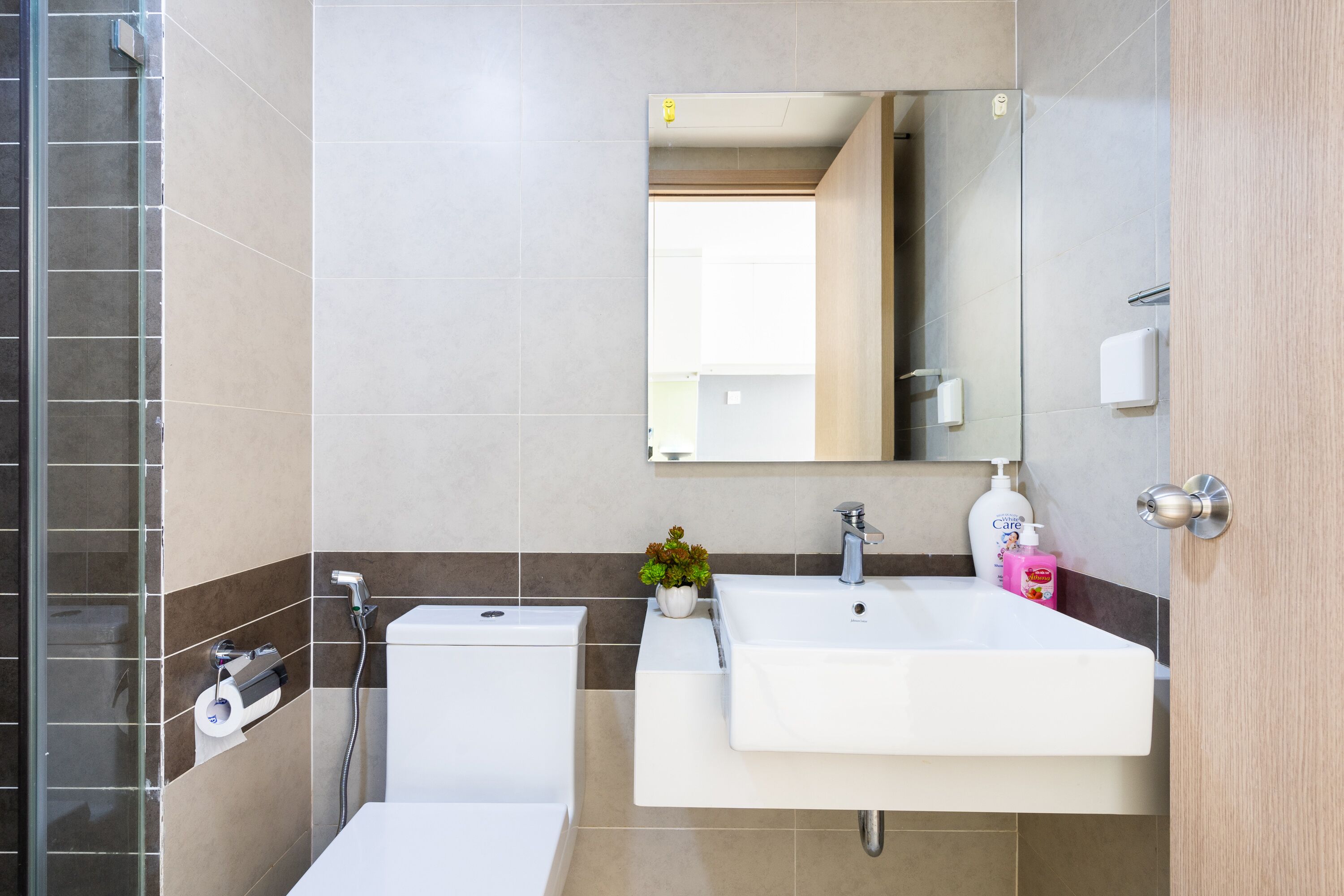 Uma casa de banho moderna com uma sanita branca, um espelho e um chuveiro.