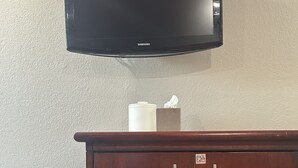 Um armário de madeira escura com duas portas, uma caixa de lenços brancos e uma televisão preta fixada numa parede com textura.