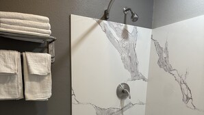 Casa de banho com sanita, chuveiro com parede de mármore e porta-toalhas com toalhas dobradas.