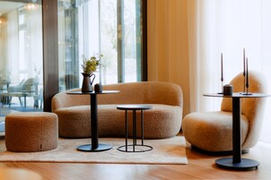 Uma área de estar moderna com um sofá, duas mesinhas e uma mesa de centro, tudo num esquema de cores neutras.