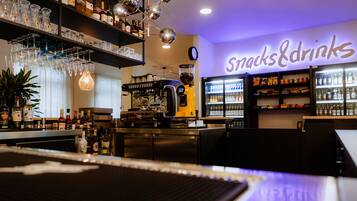 Uma área de bar com prateleiras de garrafas, uma máquina de café e um letreiro que diz 'Snacks & Drinks'.