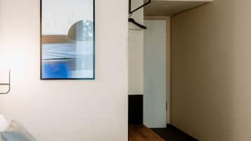 Quarto com cama, quadro na parede, luminária suspensa e porta para outro cômodo.