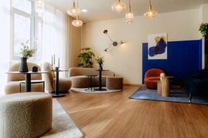 Uma sala de estar moderna com sofá, poltronas, mesa de centro e tapete. Há luminárias pendentes, um abajur na parede e uma pintura.