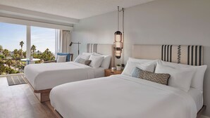 Quarto de hotel com duas camas, uma mesa de cabeceira, uma luminária e vista para o exterior.