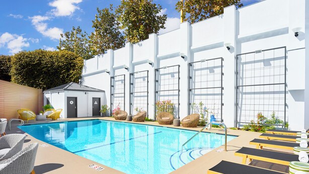 Uma piscina com espreguiçadeiras e um pequeno edifício, possivelmente um vestiário ou depósito.