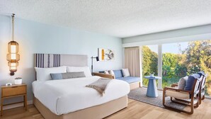 Quarto moderno com uma cama grande, mesas de cabeceira, um sofá, uma cadeira e vista para o verde.