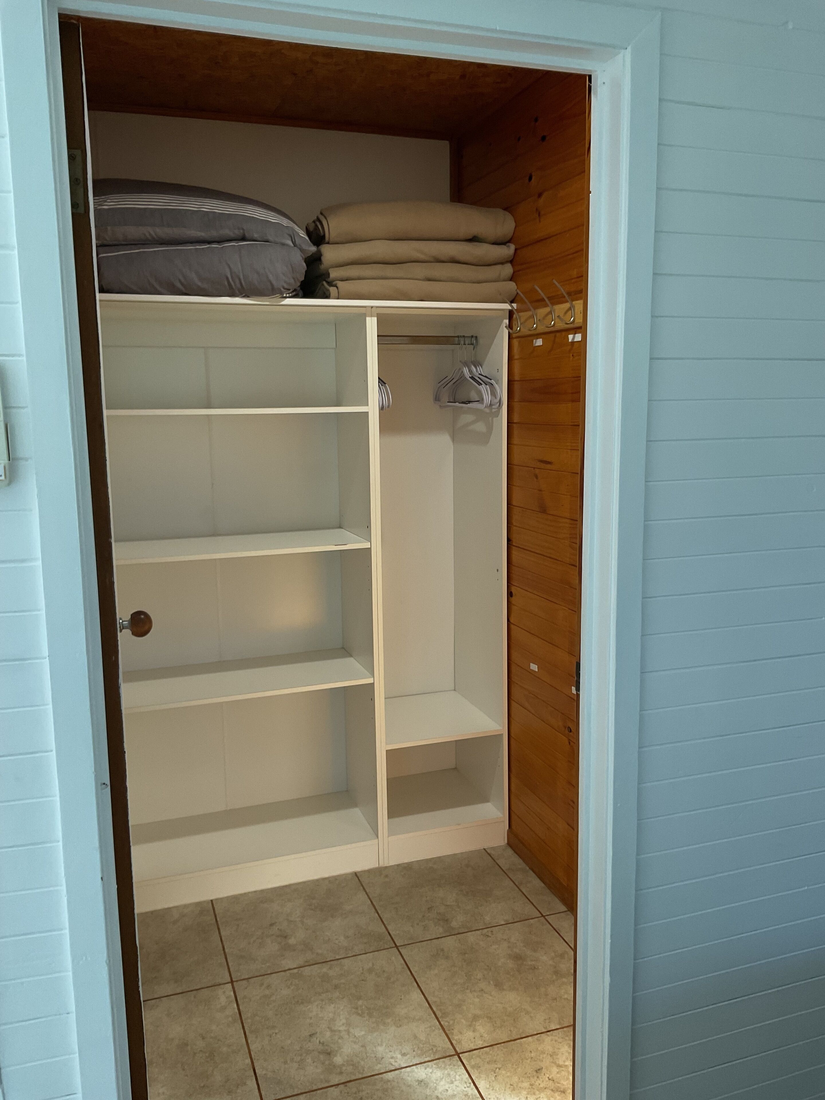Um closet espaçoso com várias prateleiras e espaço para pendurar roupas, painéis de madeira em uma parede e piso revestido.