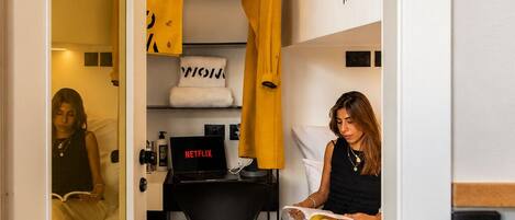 Quarto compacto com beliche, uma escrivaninha com um laptop e uma porta com a inscrição '104T'.