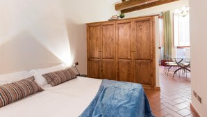 Quarto com cama, guarda-roupa de madeira e vista para uma sala de jantar.