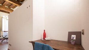 Um quarto pequeno e acolhedor com uma escrivaninha de madeira, uma garrafa vermelha, uma tigela branca e um quadro na parede.