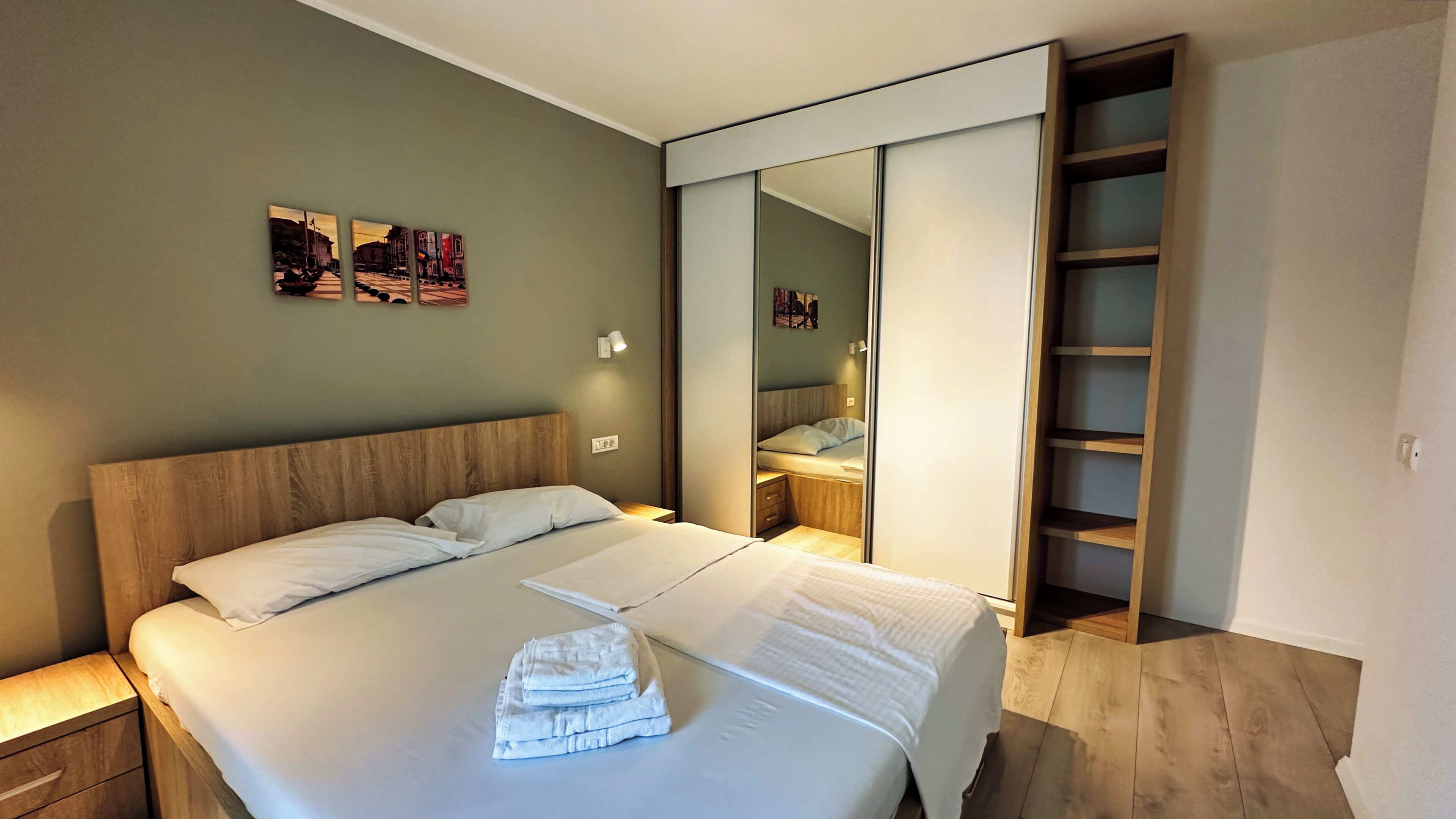 Quarto moderno com uma cama grande, cabeceira de madeira, mesa de cabeceira e um guarda-roupa embutido com espelho.
