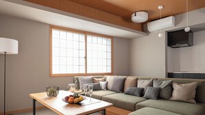 Uma sala de estar moderna com um sofá, uma mesa com frutas e copos, um abajur e uma janela grande.