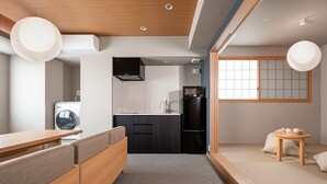 Um espaço de estar compacto com cozinha compacta, máquina de lavar roupa, área de refeições com mesa baixa e banco, e um quarto tradicional com tatames.