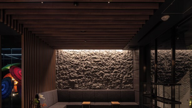 Um interior moderno com parede de pedra, ripas de madeira, um sofá cinzento e uma pequena mesa.
