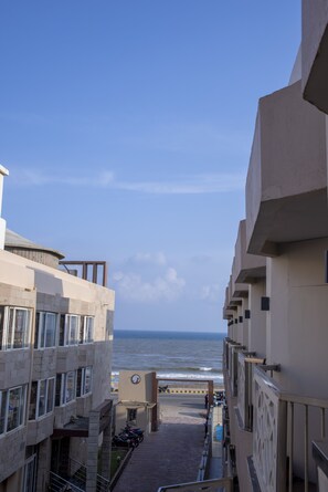 Uma passagem estreita conduz a uma praia, com vista para o oceano, ladeada por edifícios com varandas e um relógio em um deles.
