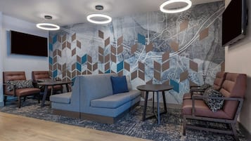 Uma área de estar moderna com sofá, poltronas e mesas, com destaque para uma parede com padrão geométrico e uma televisão de tela plana.
