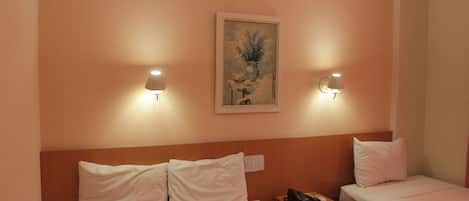 Quarto de hotel com duas camas, cada uma com roupa de cama branca, cabeceira de madeira e mesa de cabeceira com telefone e abajur.