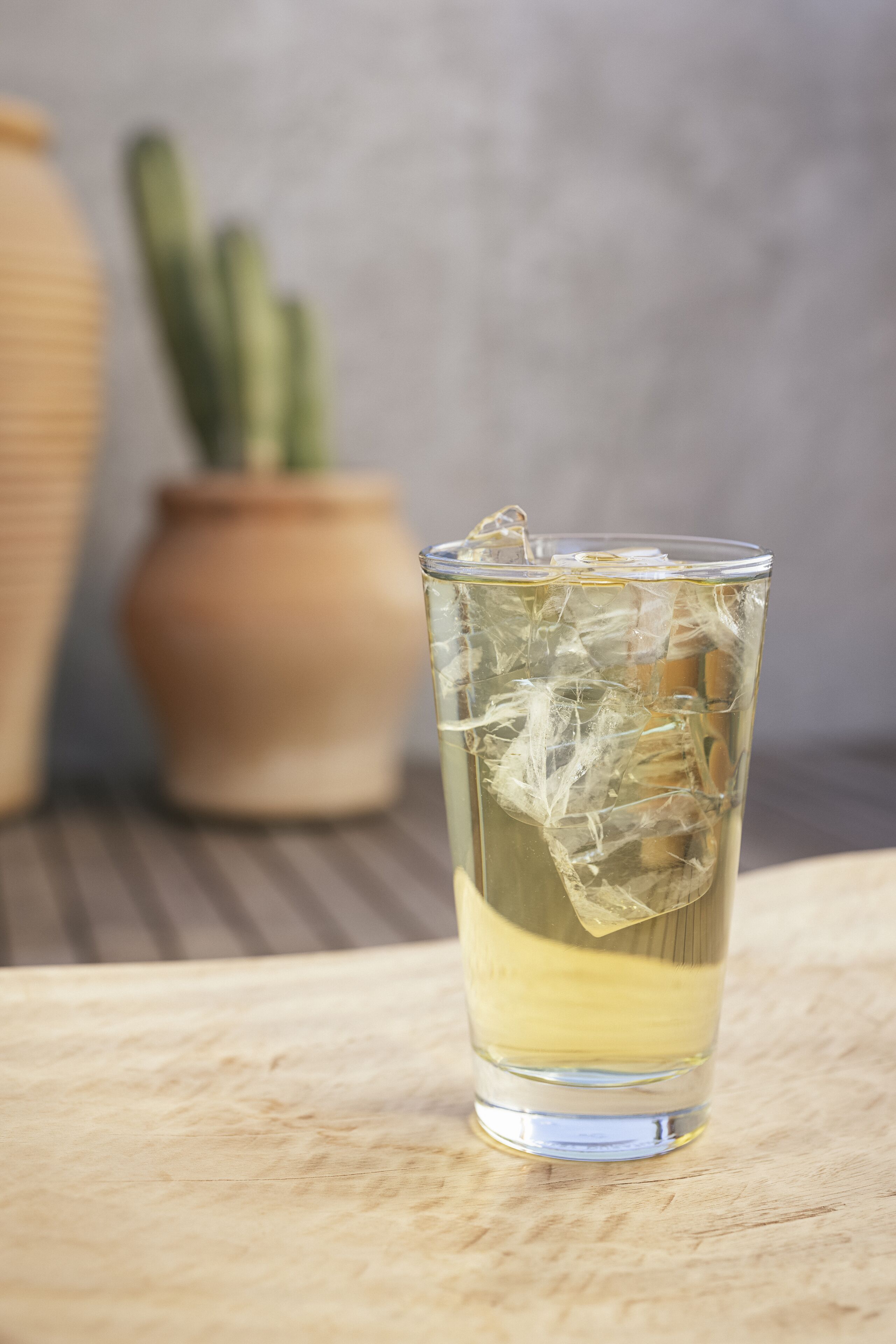 Um copo de vidro transparente com cubos de gelo e um canudo, apoiado em uma superfície de madeira.