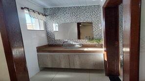 Casa de banho com lavatório de vidro, toucador de madeira, espelho e painel de azulejos.