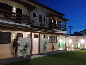 Uma casa de dois andares com varanda, plantas em vasos e entrada bem iluminada.