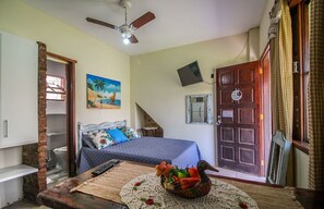 Quarto com cama, ventilador de teto, pintura, televisão e porta.