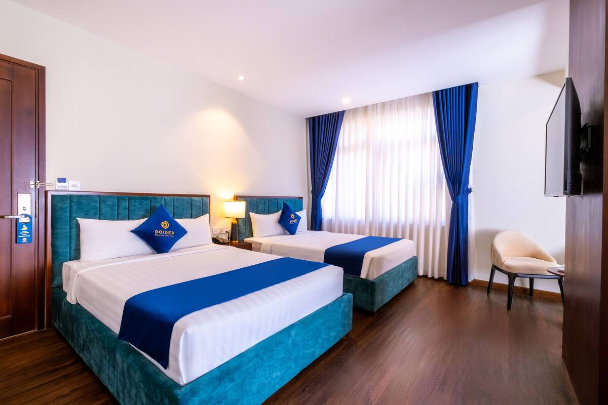 Quarto de hotel com duas camas, uma televisão, uma cadeira e uma porta de madeira.