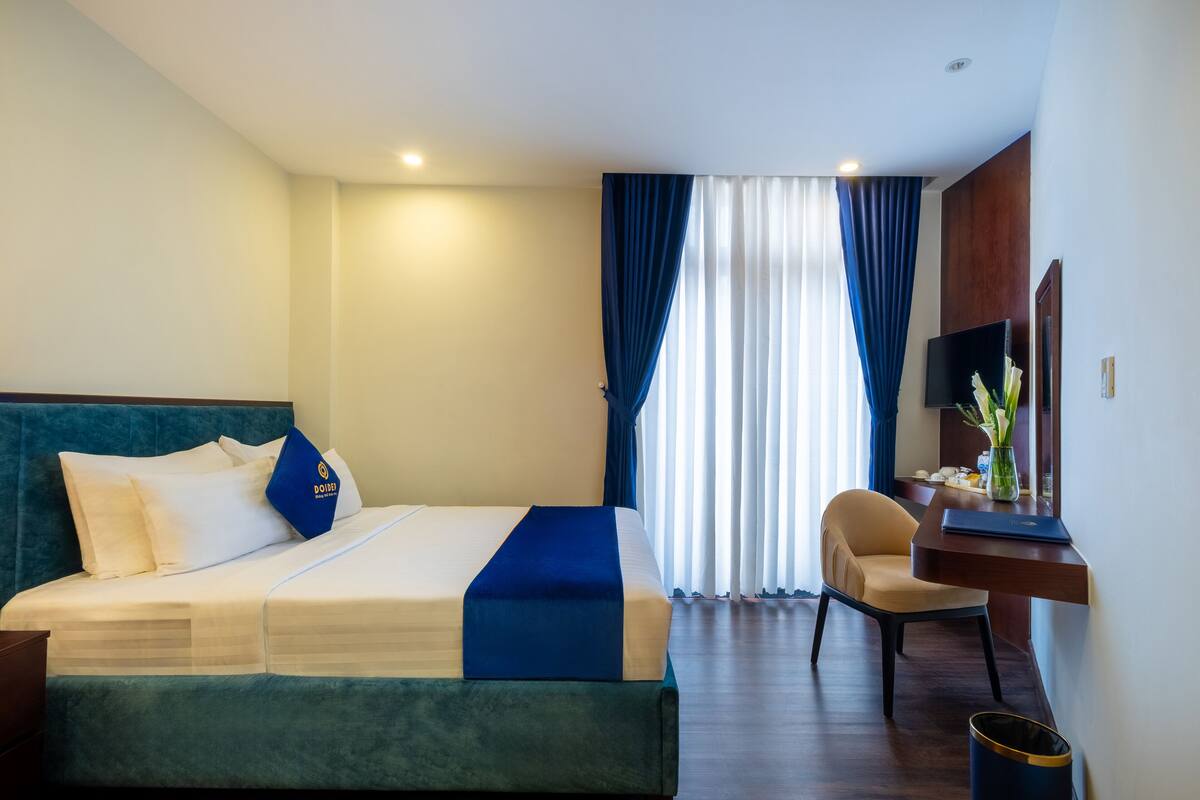 Quarto de hotel com cama, escrivaninha, cadeira e televisão.