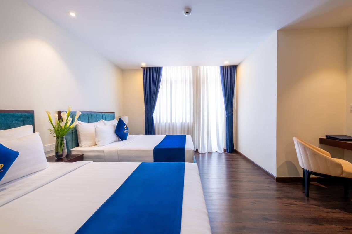 Quarto de hotel com duas camas, uma escrivaninha e uma cadeira.