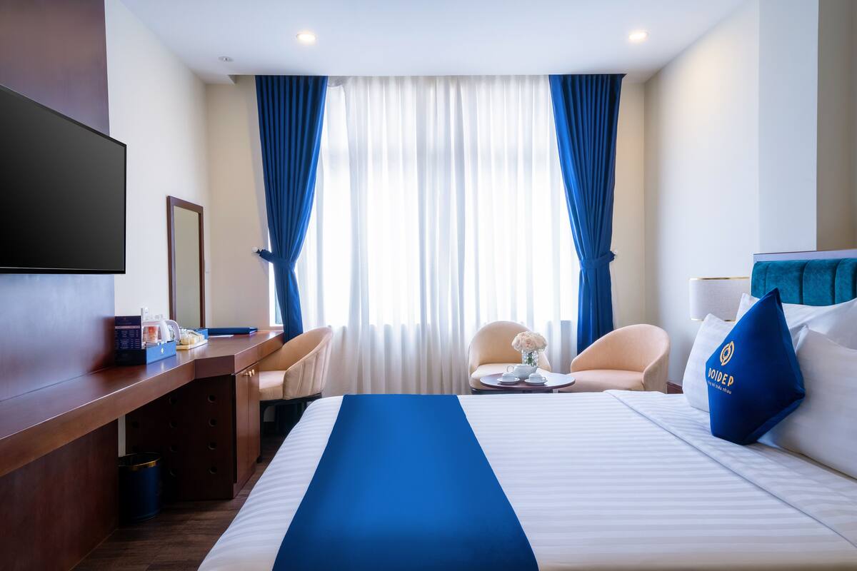 Quarto de hotel com cama grande, mesa de escritório, duas cadeiras, televisão e janela com cortinas.