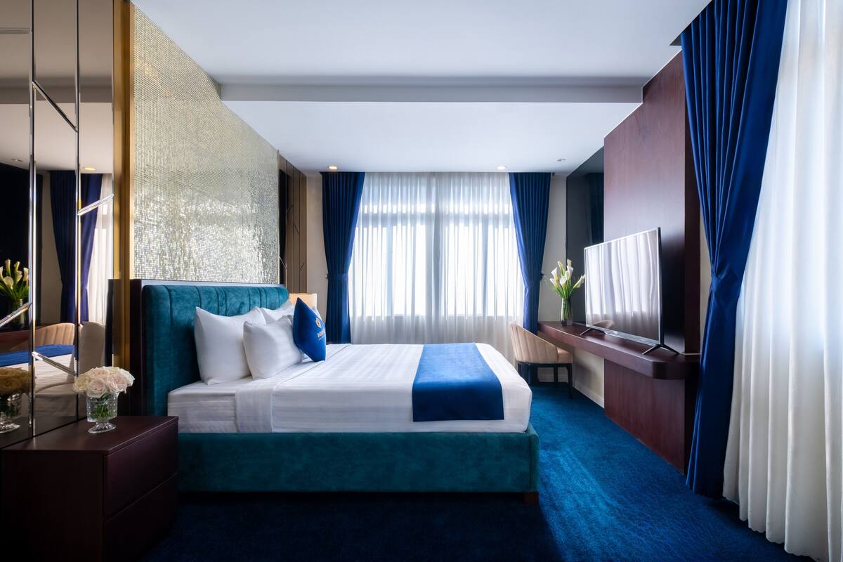 Quarto de hotel com uma cama grande, televisão, escrivaninha e espelho.