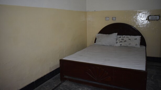 Uma cama de solteiro com cabeceira de madeira num quarto com paredes amarelas e chão de azulejos.