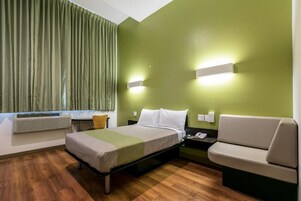 Quarto de hotel com cama, poltrona, escrivaninha e janela com cortinas.