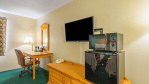 Quarto de hotel com escrivaninha, cadeira, televisão, frigorífico e espelho.
