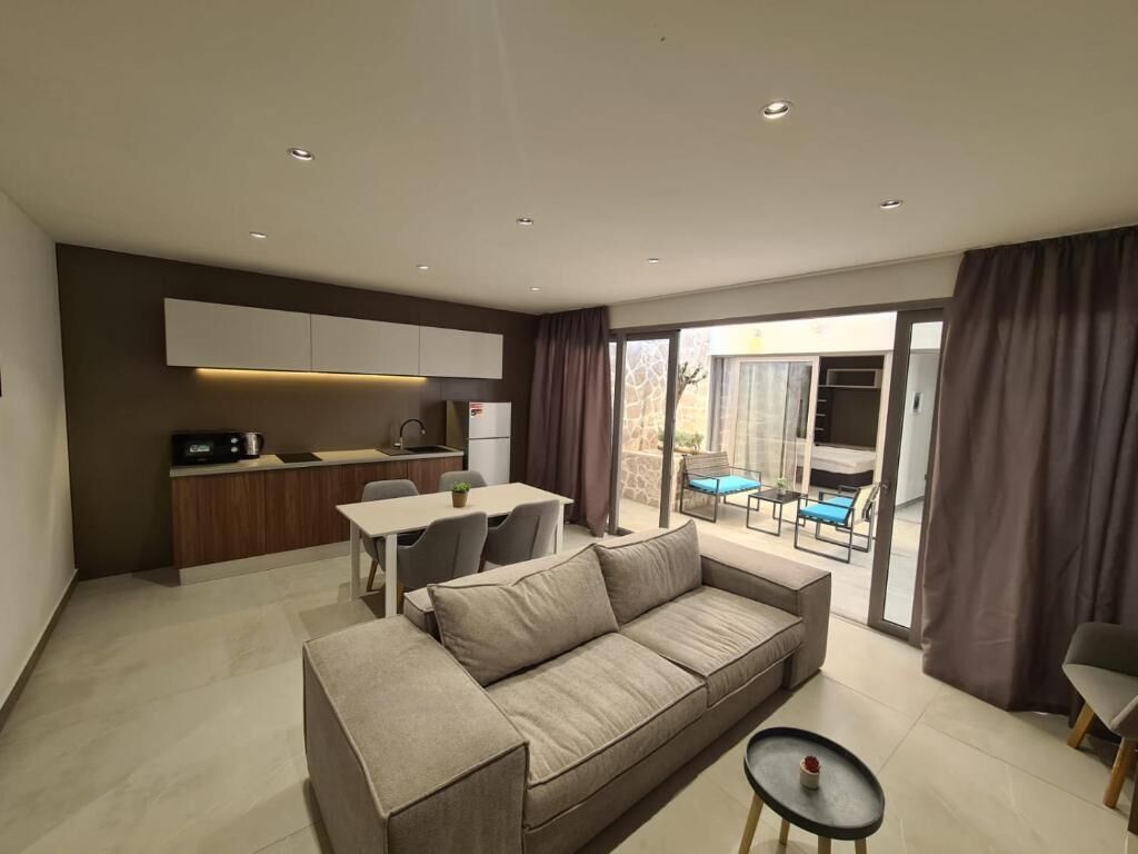 Uma sala de estar moderna com um sofá, uma mesinha e uma área de cozinha ao fundo.