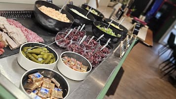 Buffet com diversos alimentos, incluindo carnes, picles e acompanhamentos.