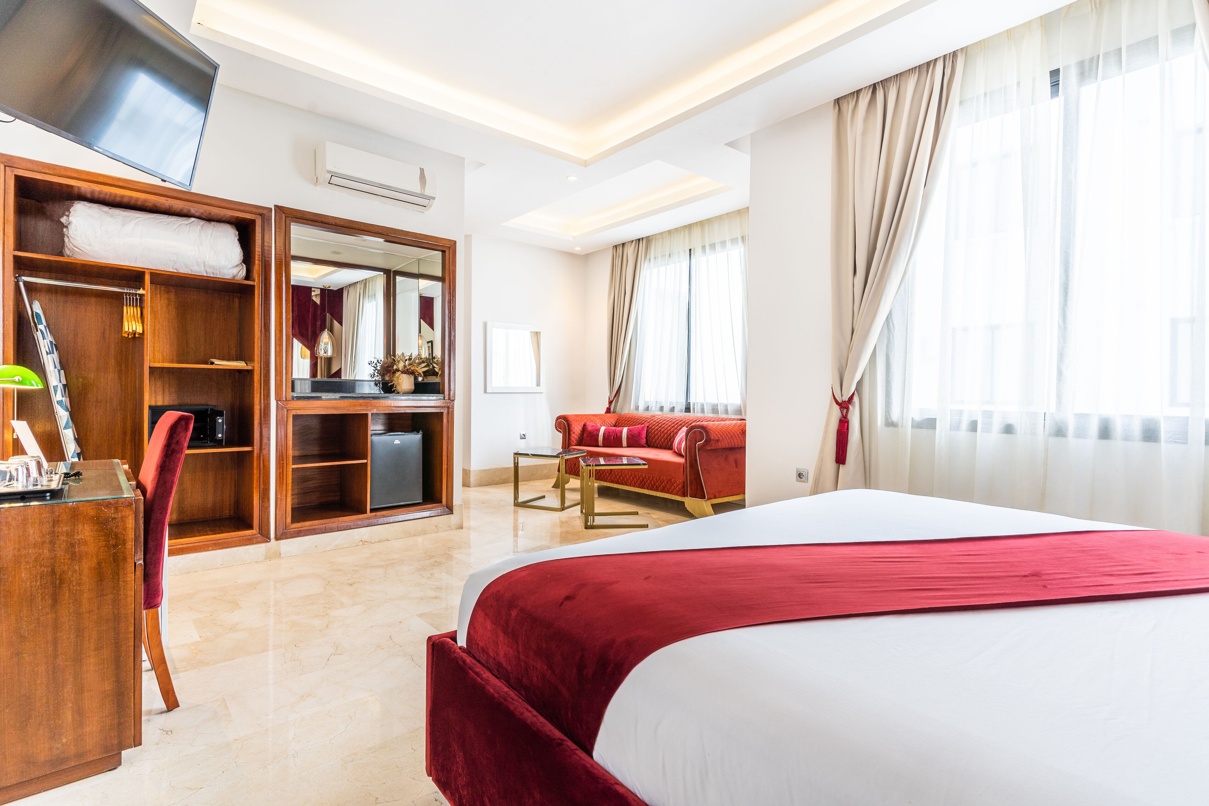Quarto de hotel com uma cama grande, uma escrivaninha, um guarda-roupa, um sofá e uma televisão.