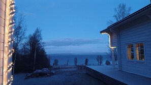 Uma casa com vista para o oceano, um quintal coberto de neve e luzes de Natal na lateral.