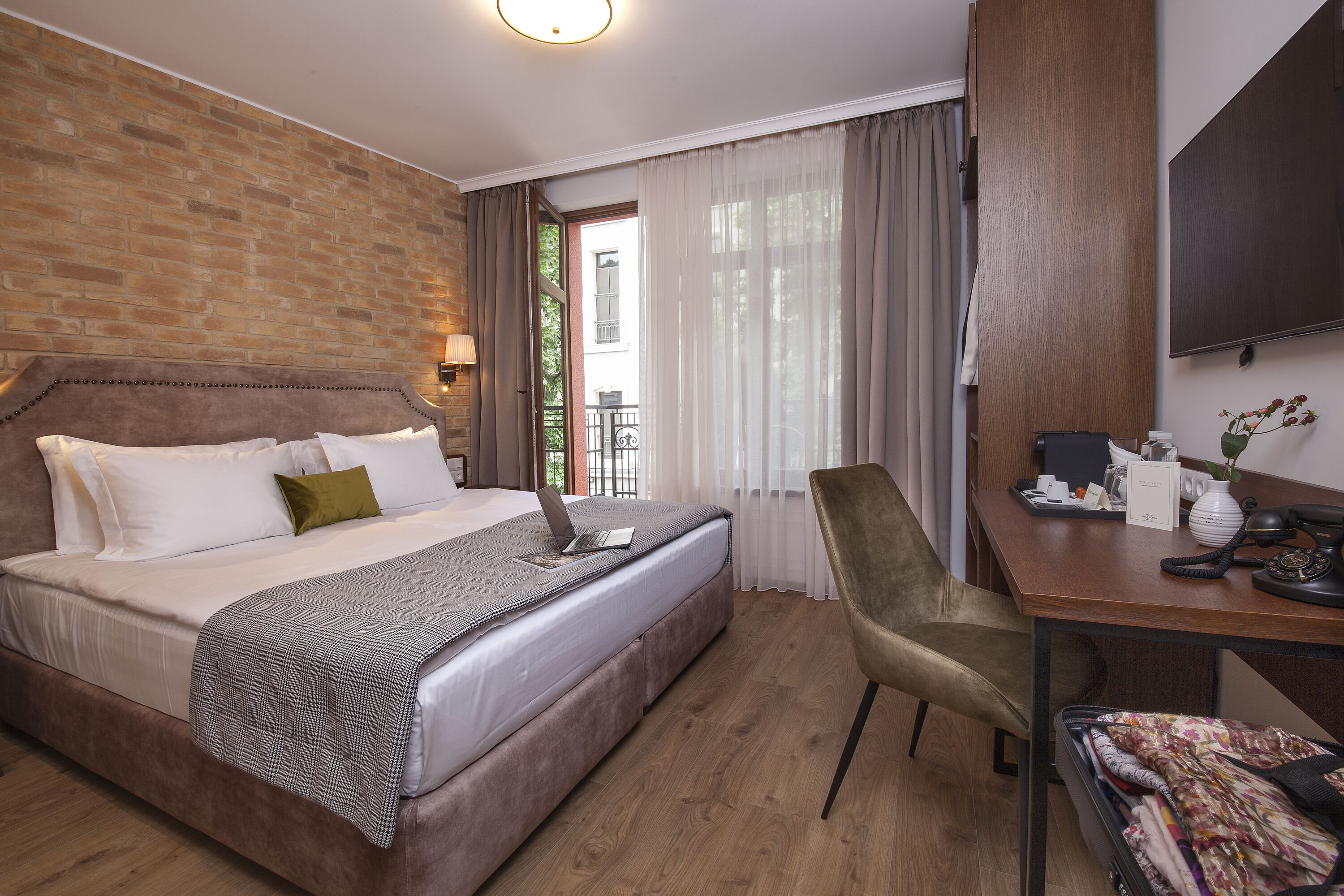 Quarto de hotel com uma cama grande, uma escrivaninha, uma cadeira e uma mala.