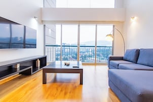 Uma sala de estar moderna com uma televisão de tela plana, um sofá, uma mesa de centro e uma varanda com vista para a cidade.