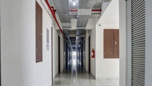 Um corredor comprido e estreito com chão de azulejos brancos e portas em ambos os lados.