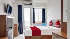 Quarto de hotel com cama, televisão, secretária e janela com cortinas.