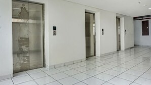 Um corredor limpo e moderno com três portas de elevador, piso de azulejos brancos e uma parede lisa.