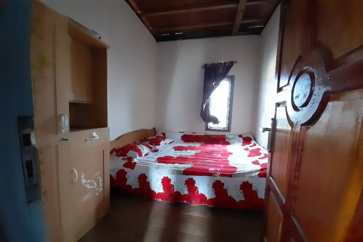 Quarto com cama, guarda-roupa de madeira, janela com cortinas e porta com puxador redondo.