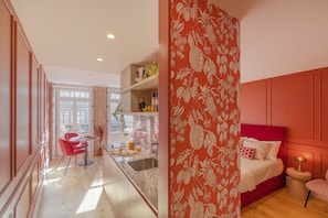 Quarto moderno com cabeceira vermelha, mesa de cabeceira com abajur e vista da cidade através de grandes janelas.