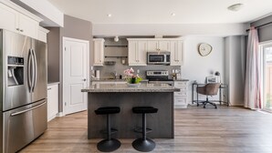 Uma cozinha moderna com eletrodomésticos de aço inoxidável, uma ilha central com banquetas e um espaço de refeições com uma cadeira.