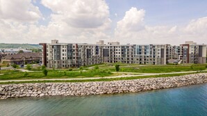 Um complexo de apartamentos moderno com vários andares, varandas e um rio ao primeiro plano.