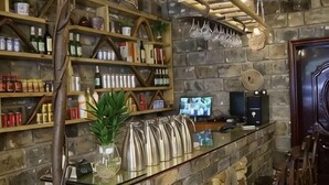 Uma área de bar com prateleiras cheias de garrafas, um balcão de vidro e uma parede de pedra.