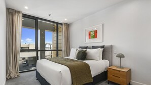 Quarto moderno com uma cama grande, uma mesa de cabeceira, uma luminária e uma janela com cortinas.