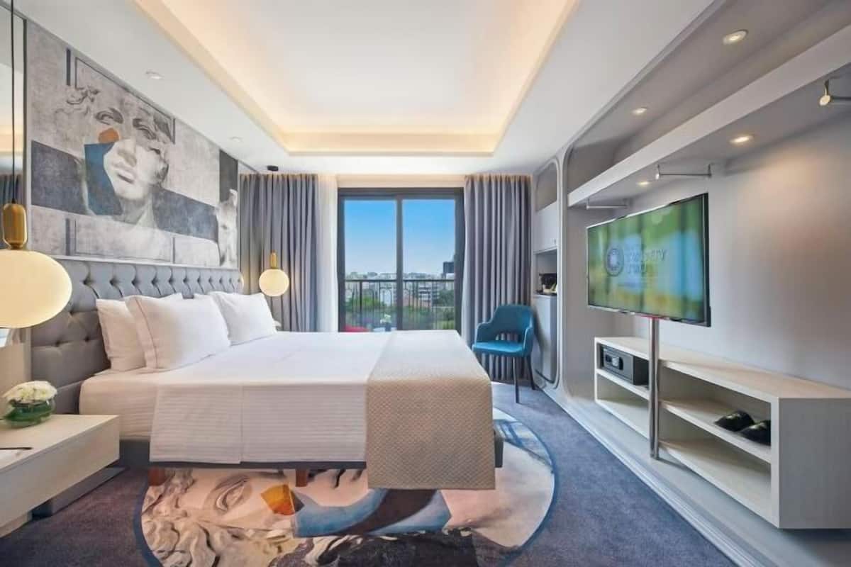 Quarto de hotel moderno com uma cama grande, televisão de tela plana, escrivaninha e vista para a cidade.