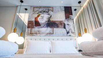 Quarto de hotel moderno com uma cama grande, um mural decorativo e iluminação pendente.